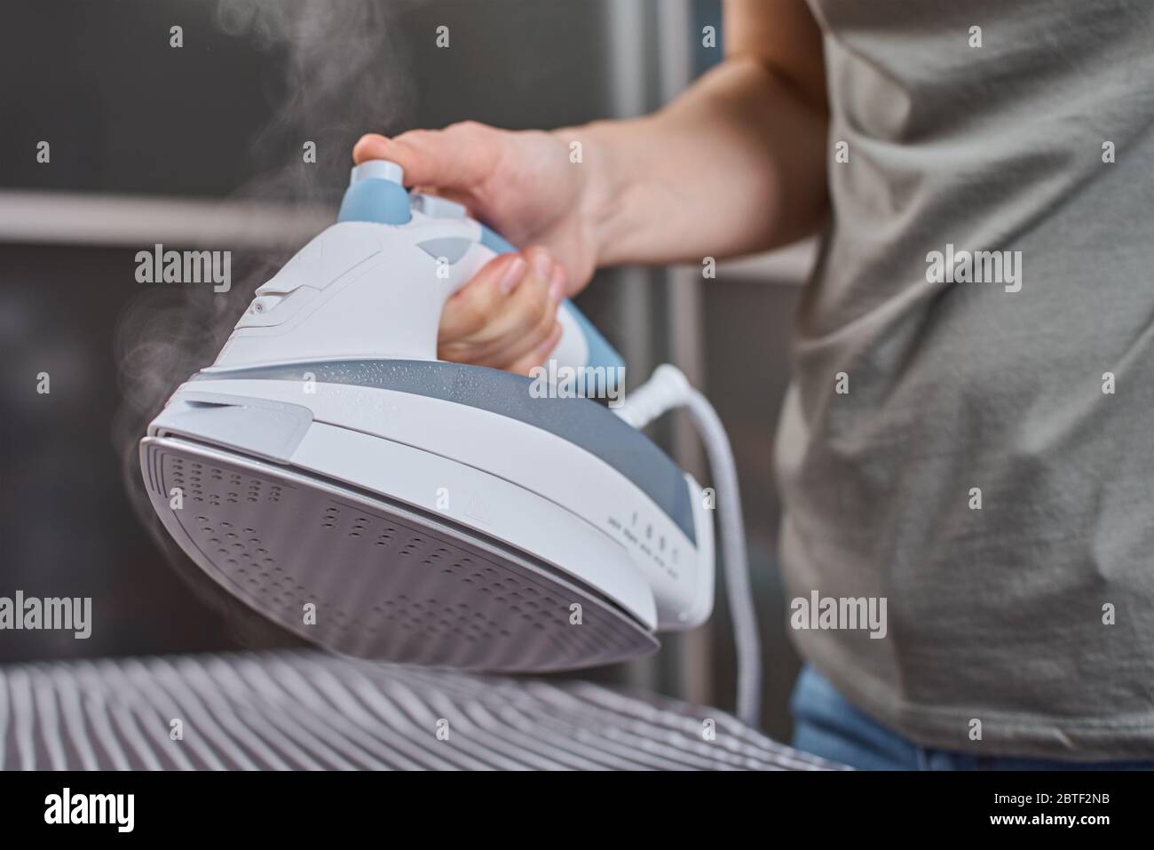 Steam boost on modern iron. Woman ironing clothes with modern iron ...