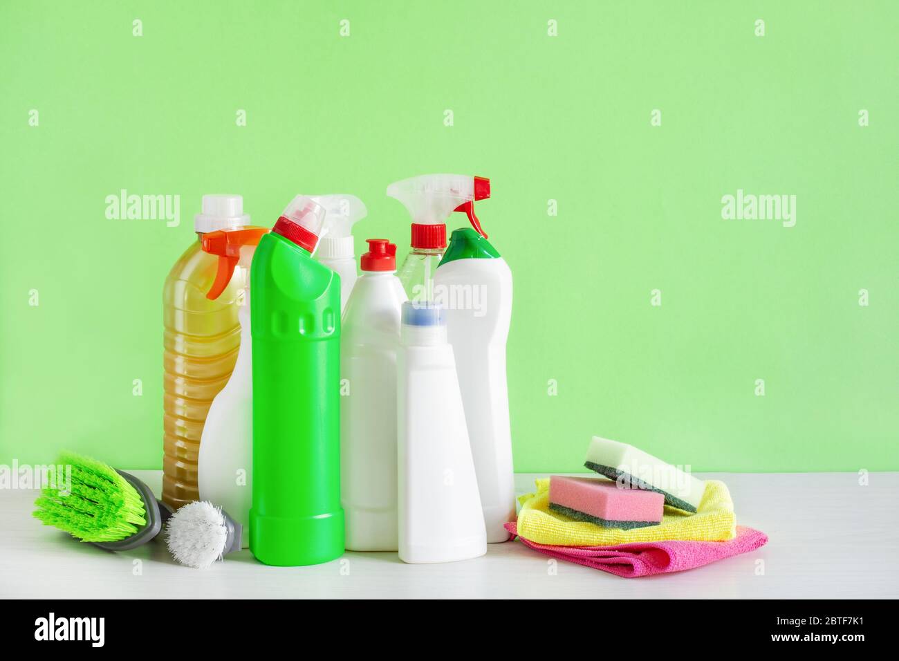 Bottles of detergent and cleaning tools over green background ...