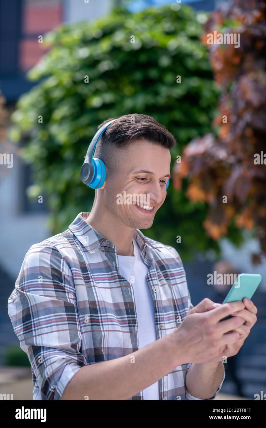 Smiling dark-haired male wearing headphones, chatting on the phone ...