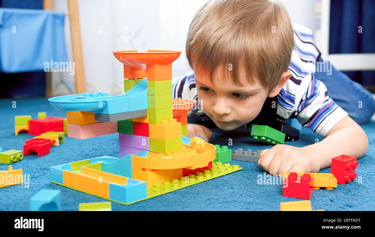 Portrait of little concentrated boy lying on floor and looking on toy ...