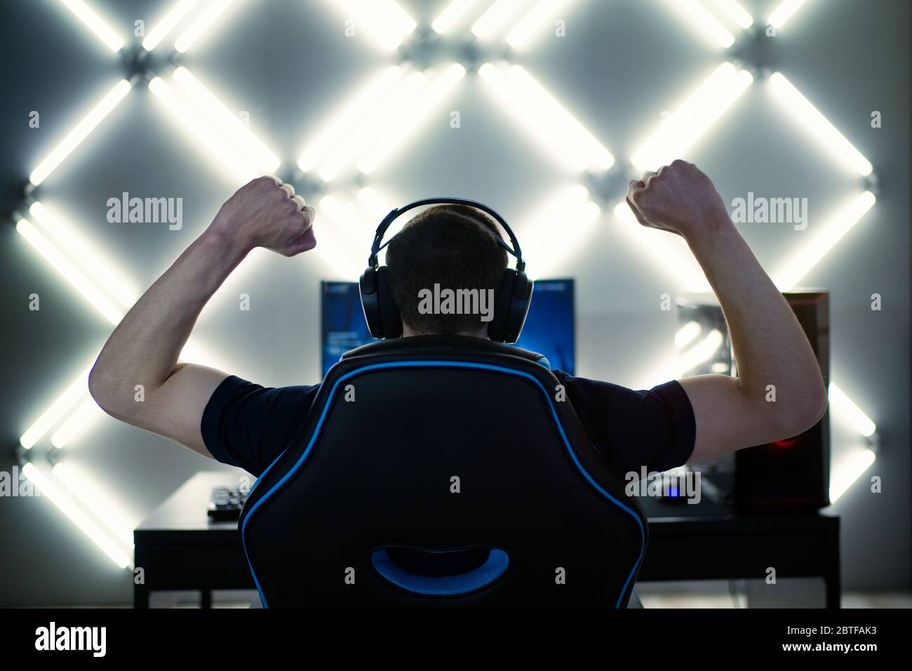 Back view of young gamer guy in headphones screaming and rejoicing ...