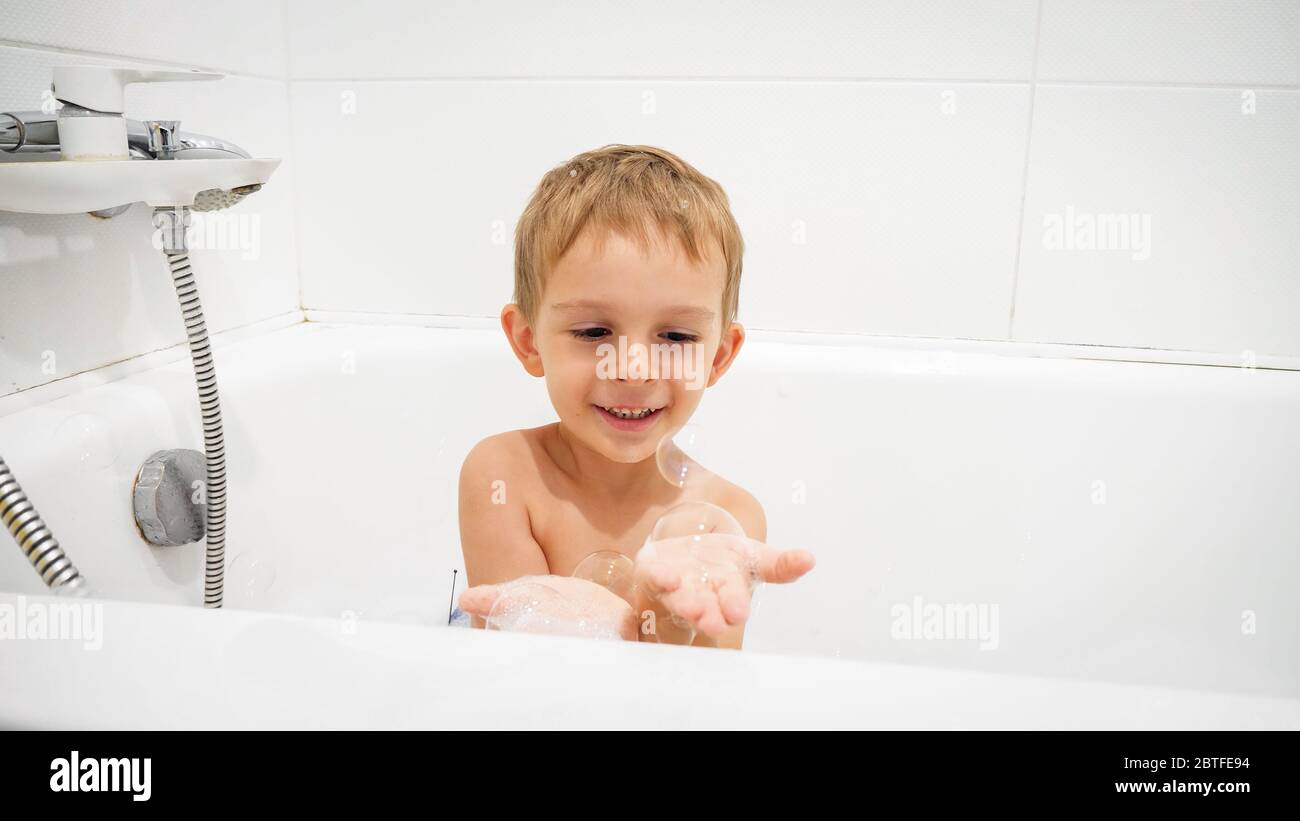Portrait of cute little boy holding soap bubbles on hand while having ...
