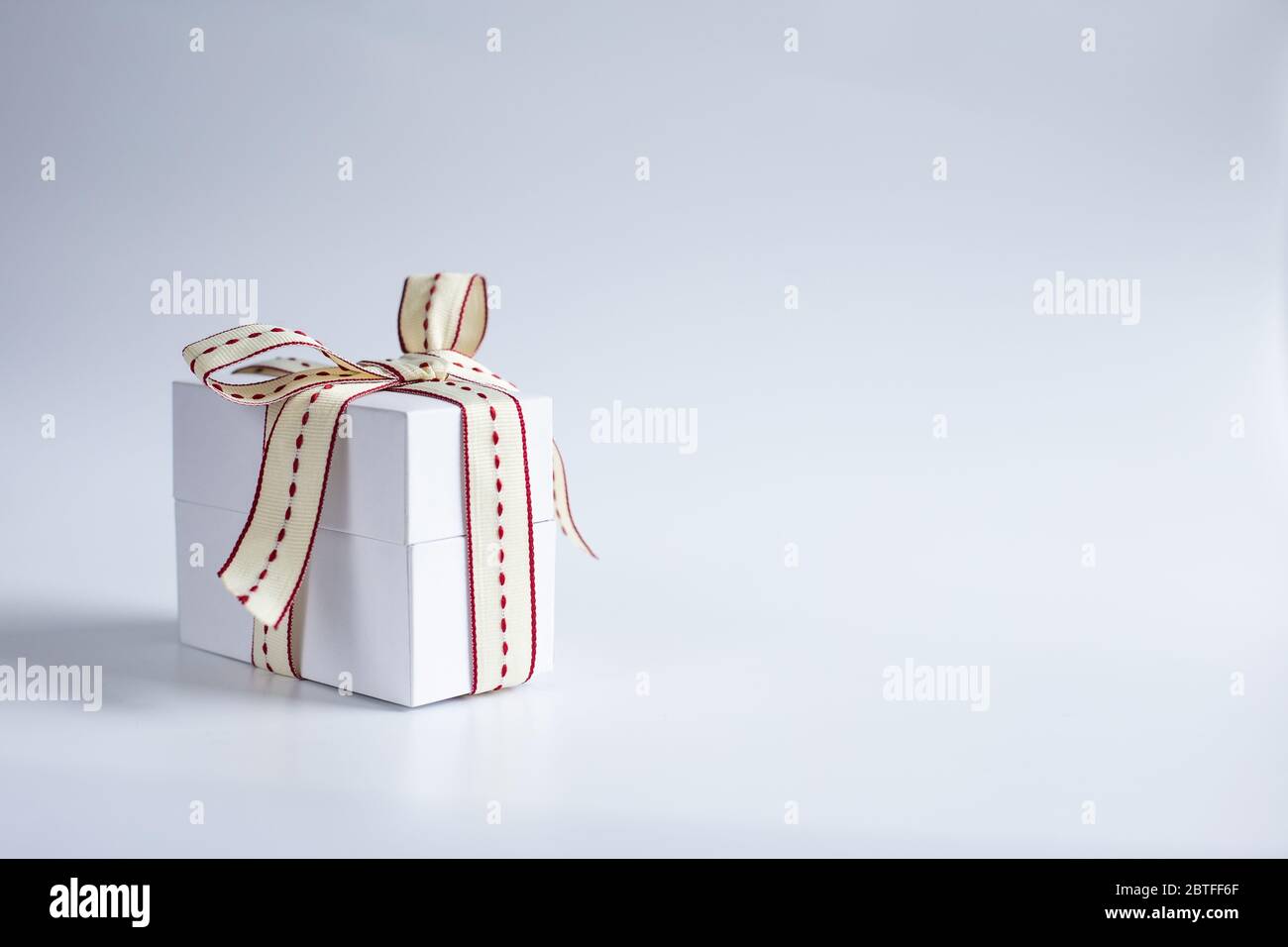 Small white gift box with dotted red and whote ribbon on white ...