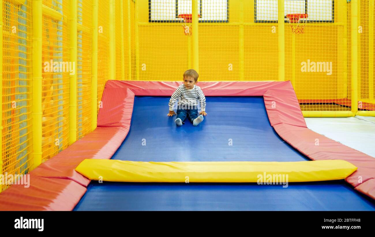 Cute little boy sliding and jumping on tramploines at playroom in ...