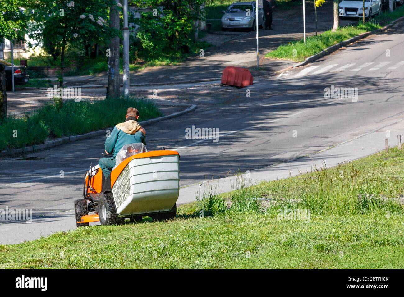 A utility worker takes care of roadside lawns, mowing tall grass with a ...