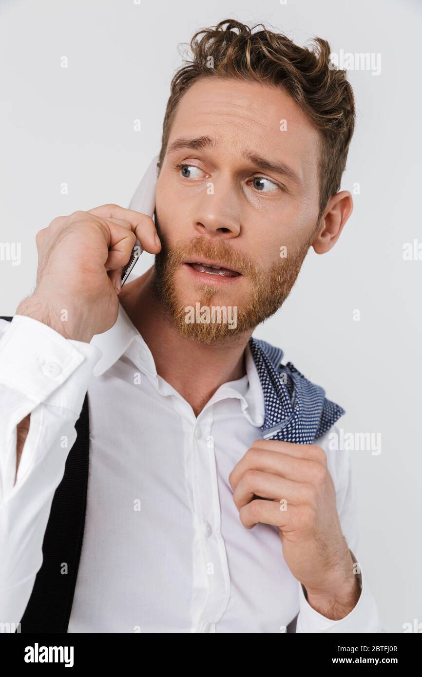 Image of confused blonde man holding jacket and talking on cellphone ...