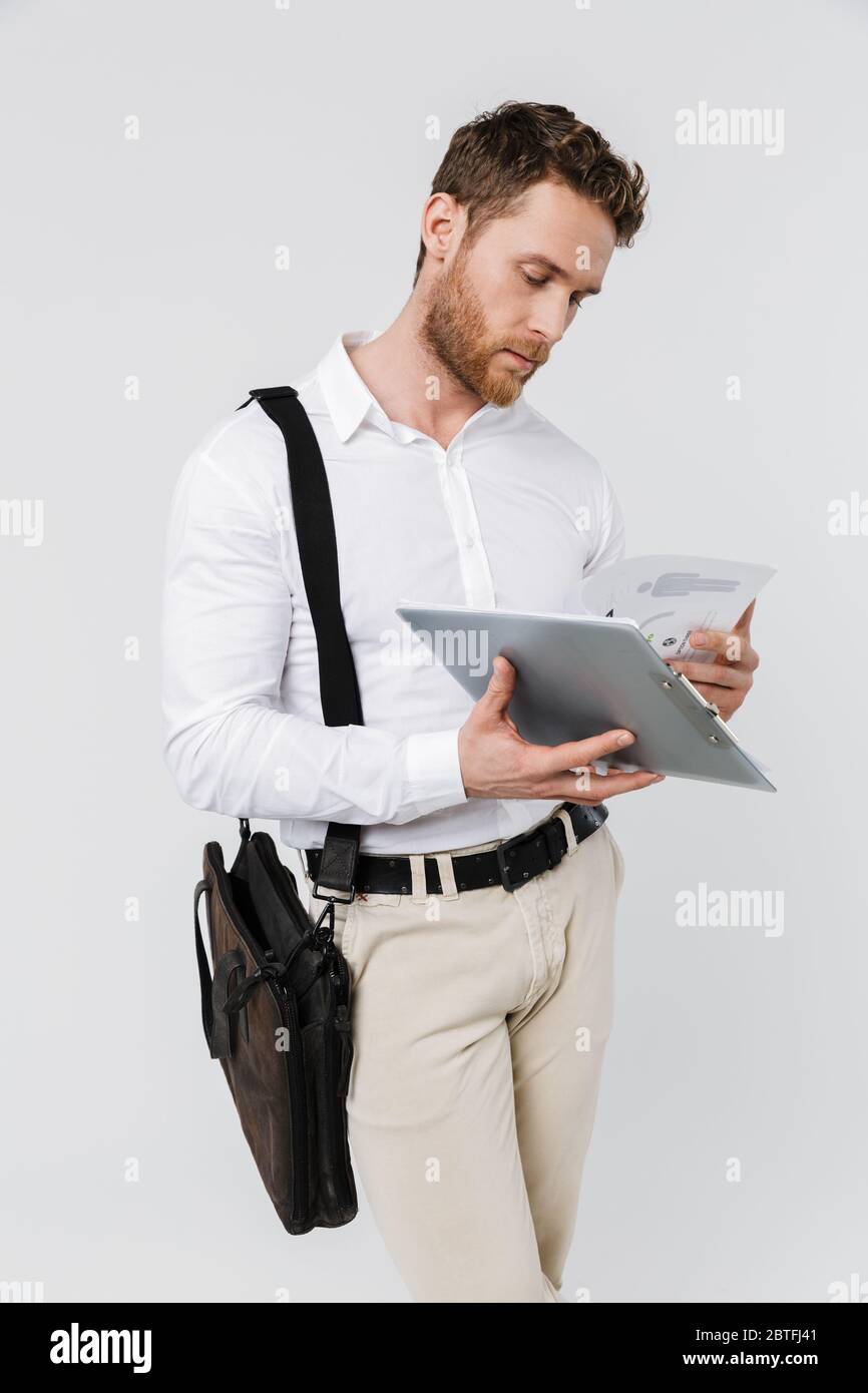 Image of concentrated young man holding clipboard and reading documents ...