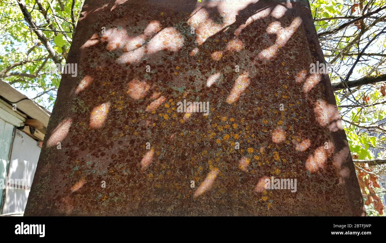 Dirty weathered brown rusty metal surface with blurry spots of sunlight ...