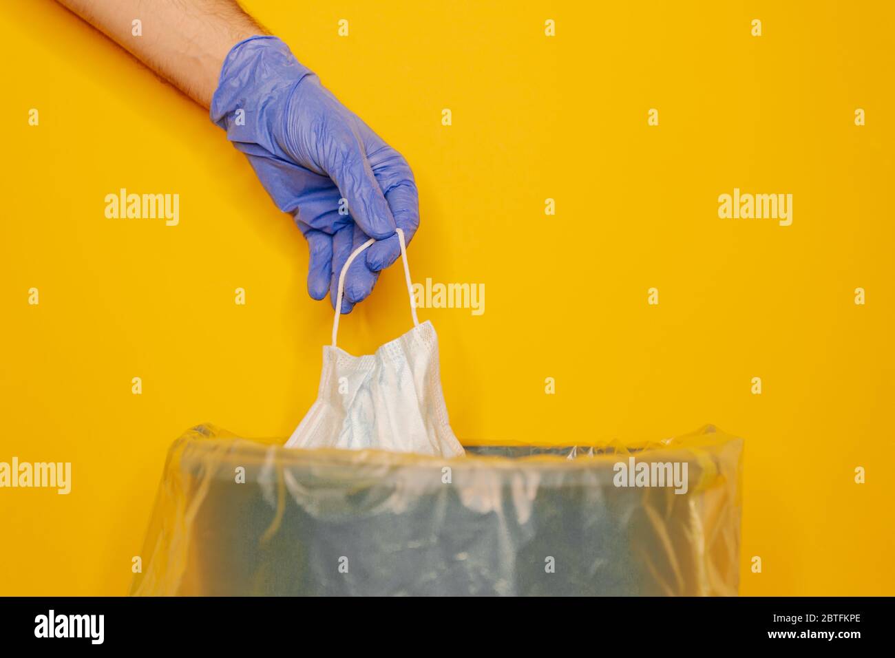 The blue latex gloved hand putting the surgical mask in the trash, on ...