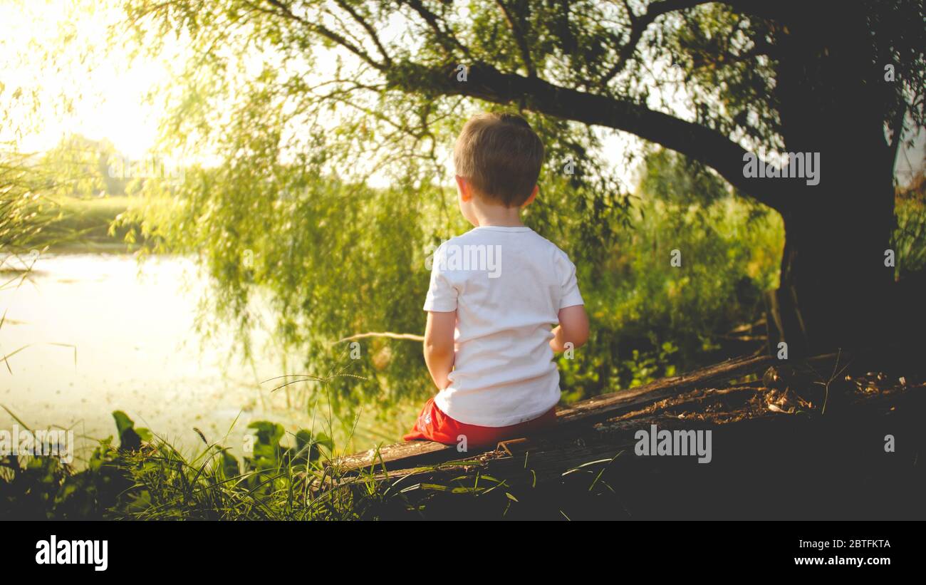 Toned rear view photo of little boy fishing on the river at sunset ...