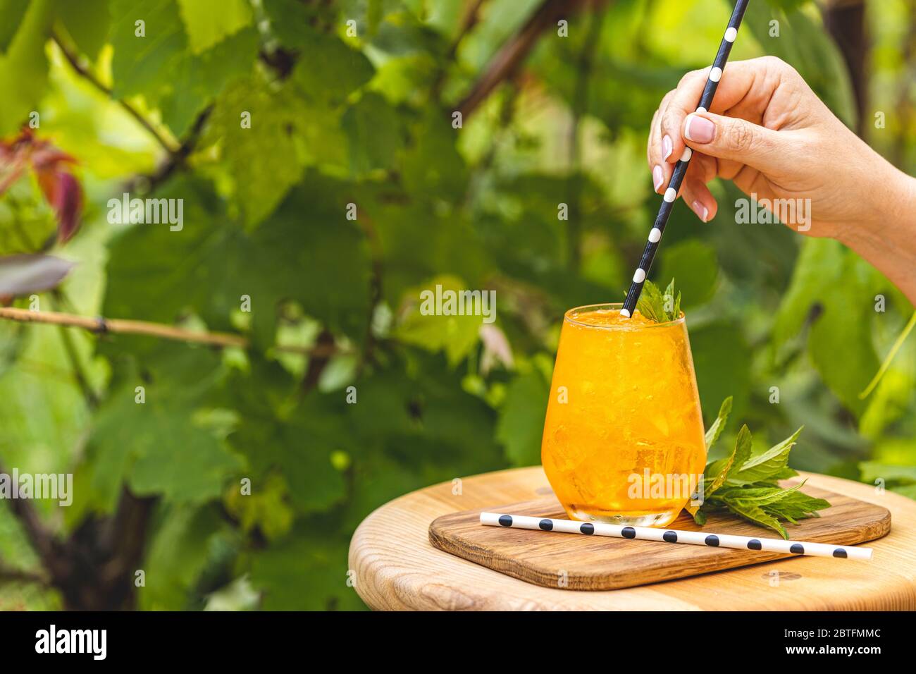 Woman hand holding drinking straw over orange drink with ice on summer ...