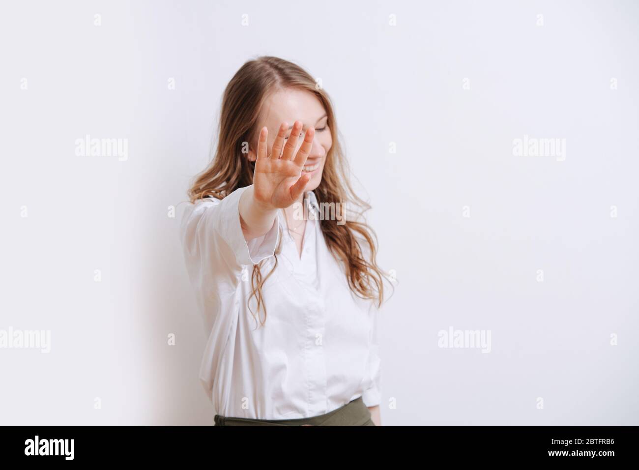 Shy young woman blocking camera with her hand. Over white background ...