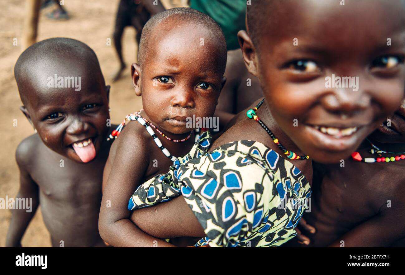 TOPOSA TRIBE, SOUTH SUDAN - MARCH 12, 2020: Girl smiling and carrying ...