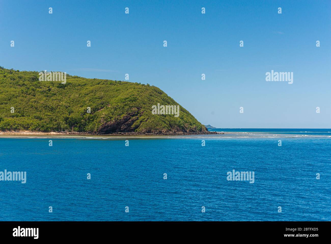 Green island with a forest ends at deep blue water. Fiji Yasawa islands ...