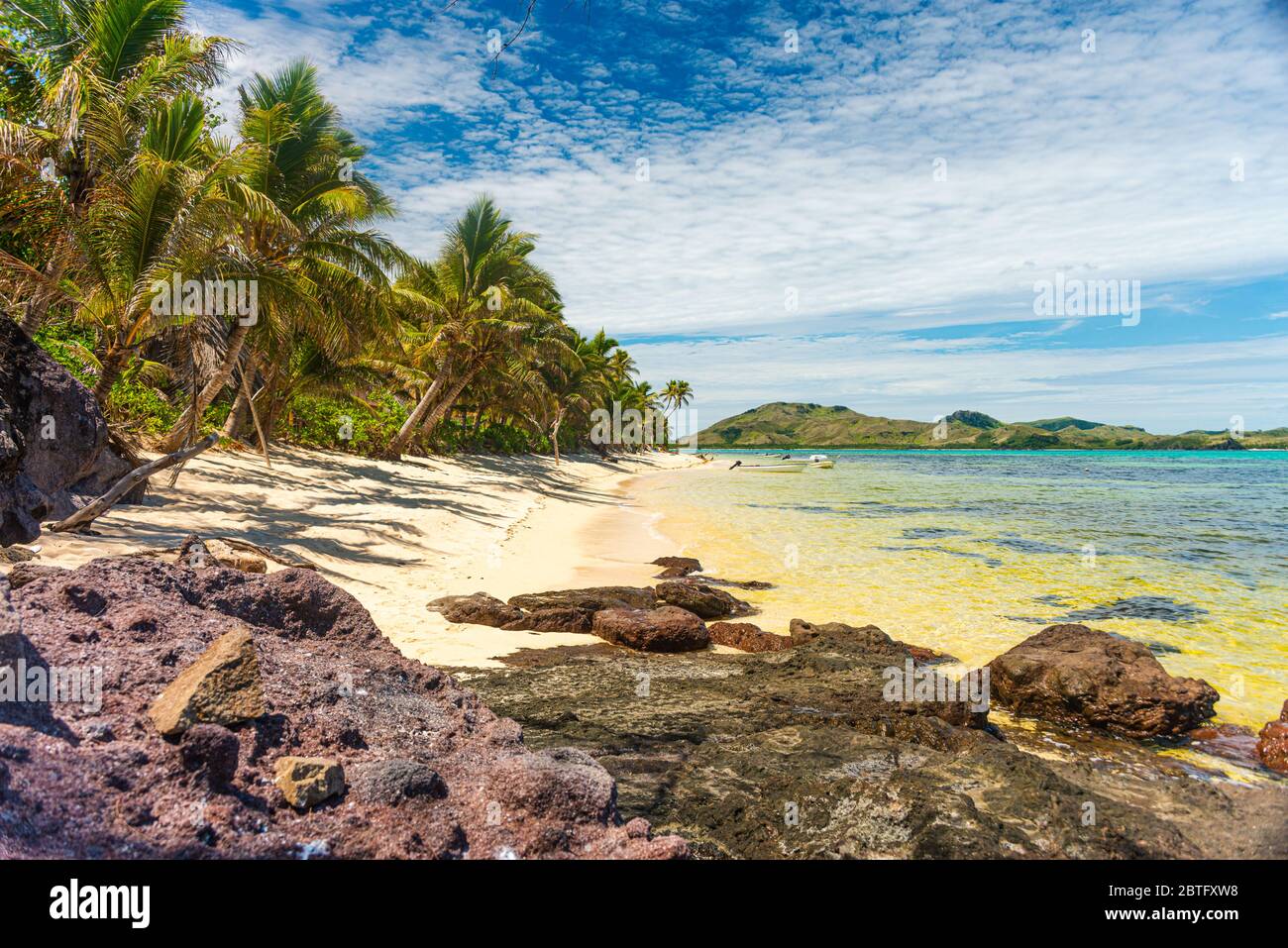 White sandy beach with rocks in the foreground. Palm trees and clear ...