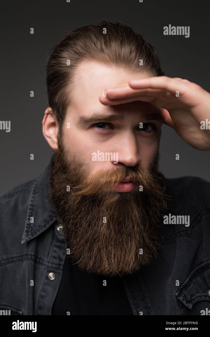 Young hipster man with long perfect beard looking far away on gray ...