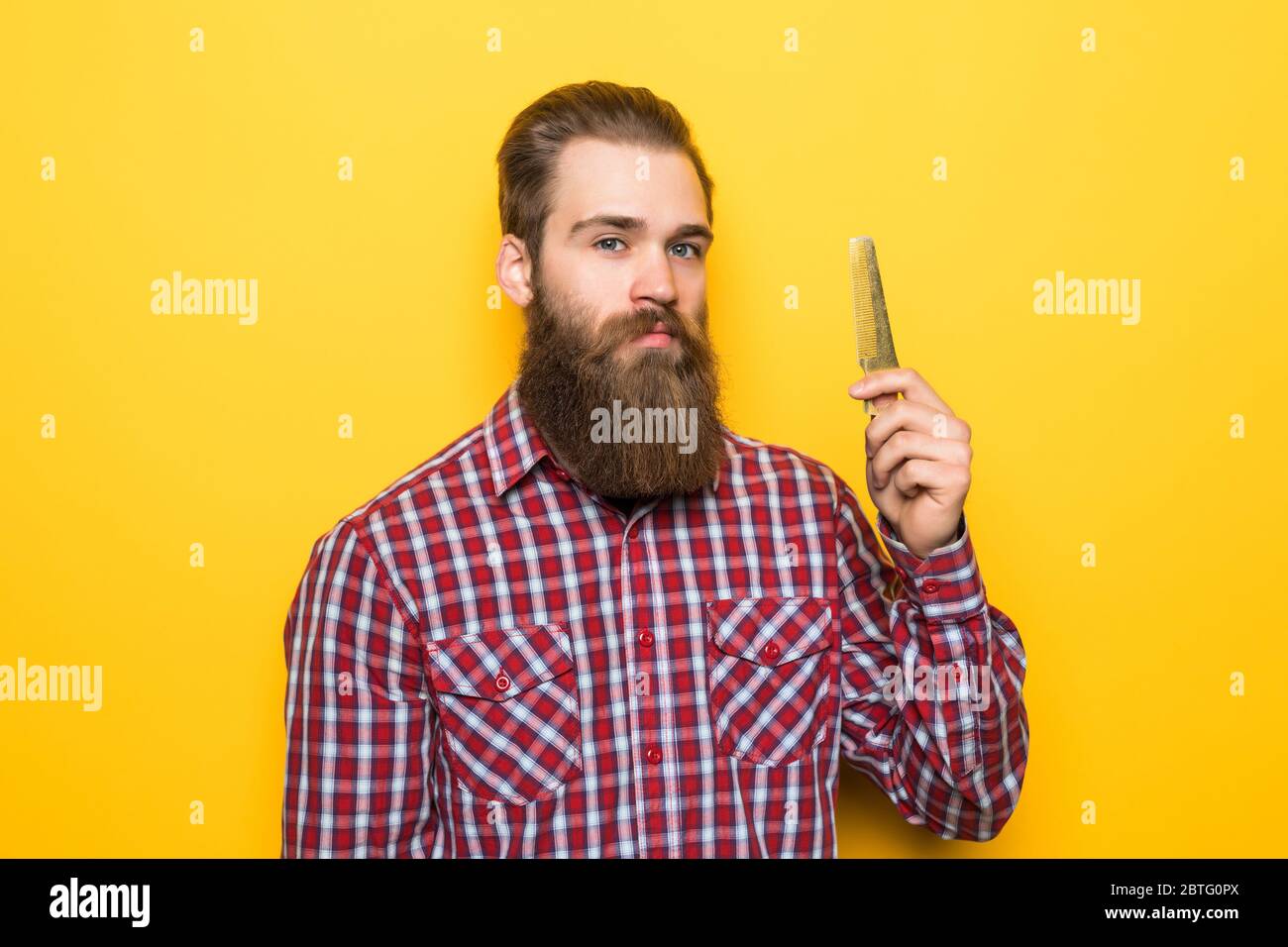 Happy hipster man comb his beard and moustache on yellow background ...