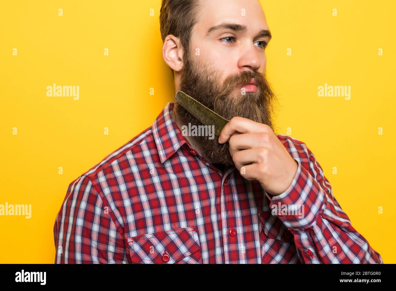 Happy hipster man comb his beard and moustache on yellow background ...