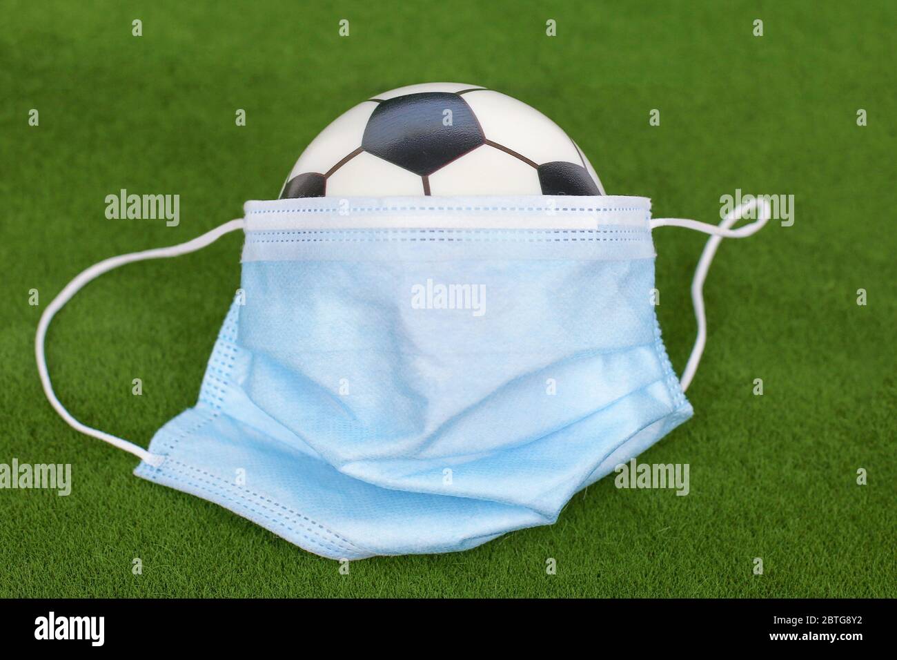 Soccer ball in a medical mask on a green background. Cancellation of ...