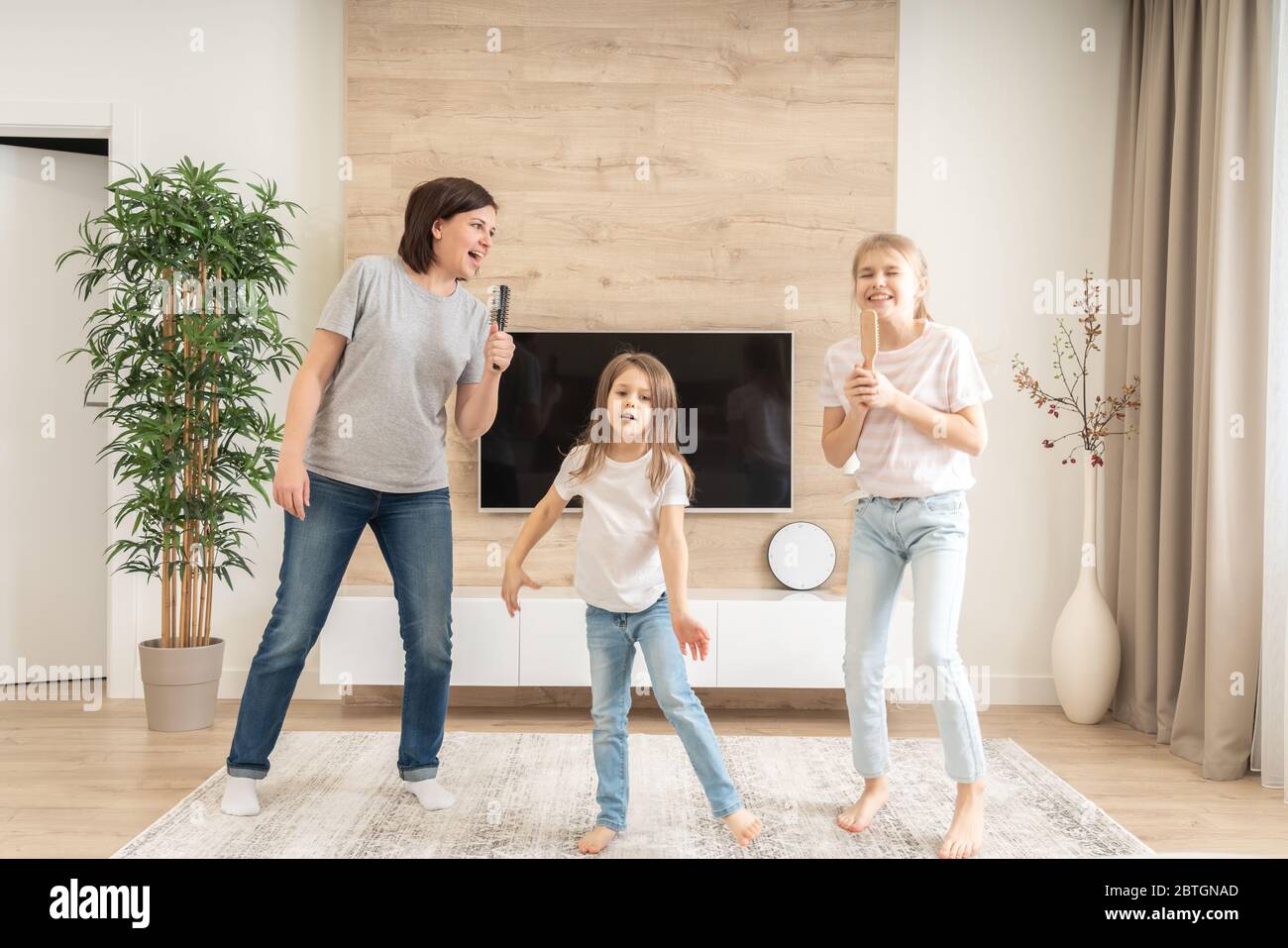 Happy mother and two daughters having fun singing karaoke song in hairbrushes. mother laughing ...