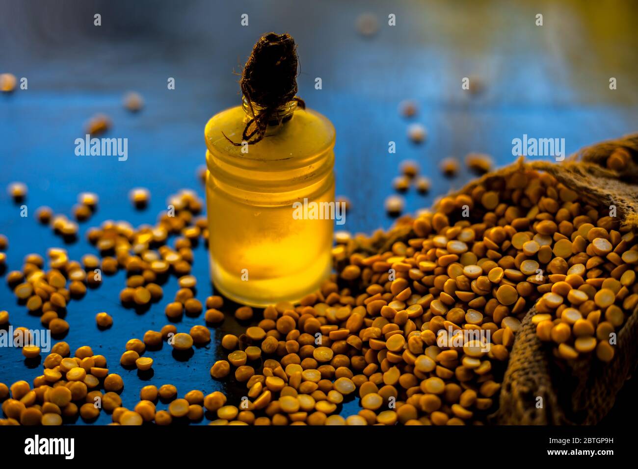 Close up of refined chickpea oil in a glass bottle on a glossy black ...