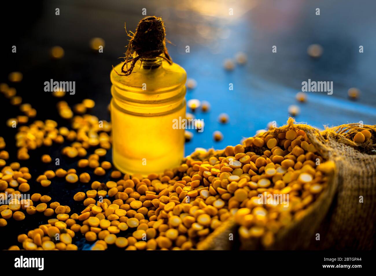Close up of refined chickpea oil in a glass bottle on a glossy black ...