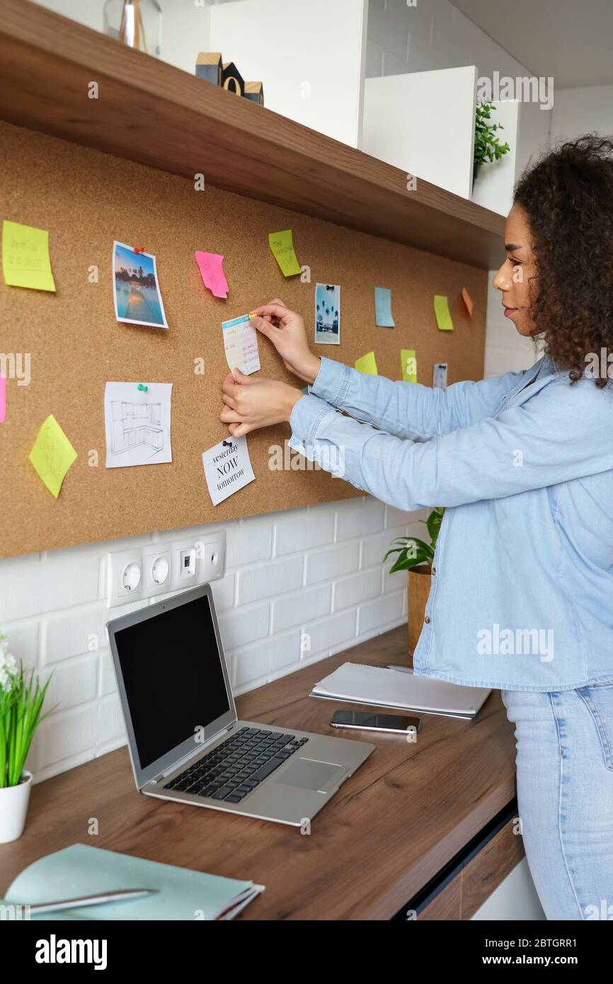 African woman pin weekly planning sticker on mood board at home office ...