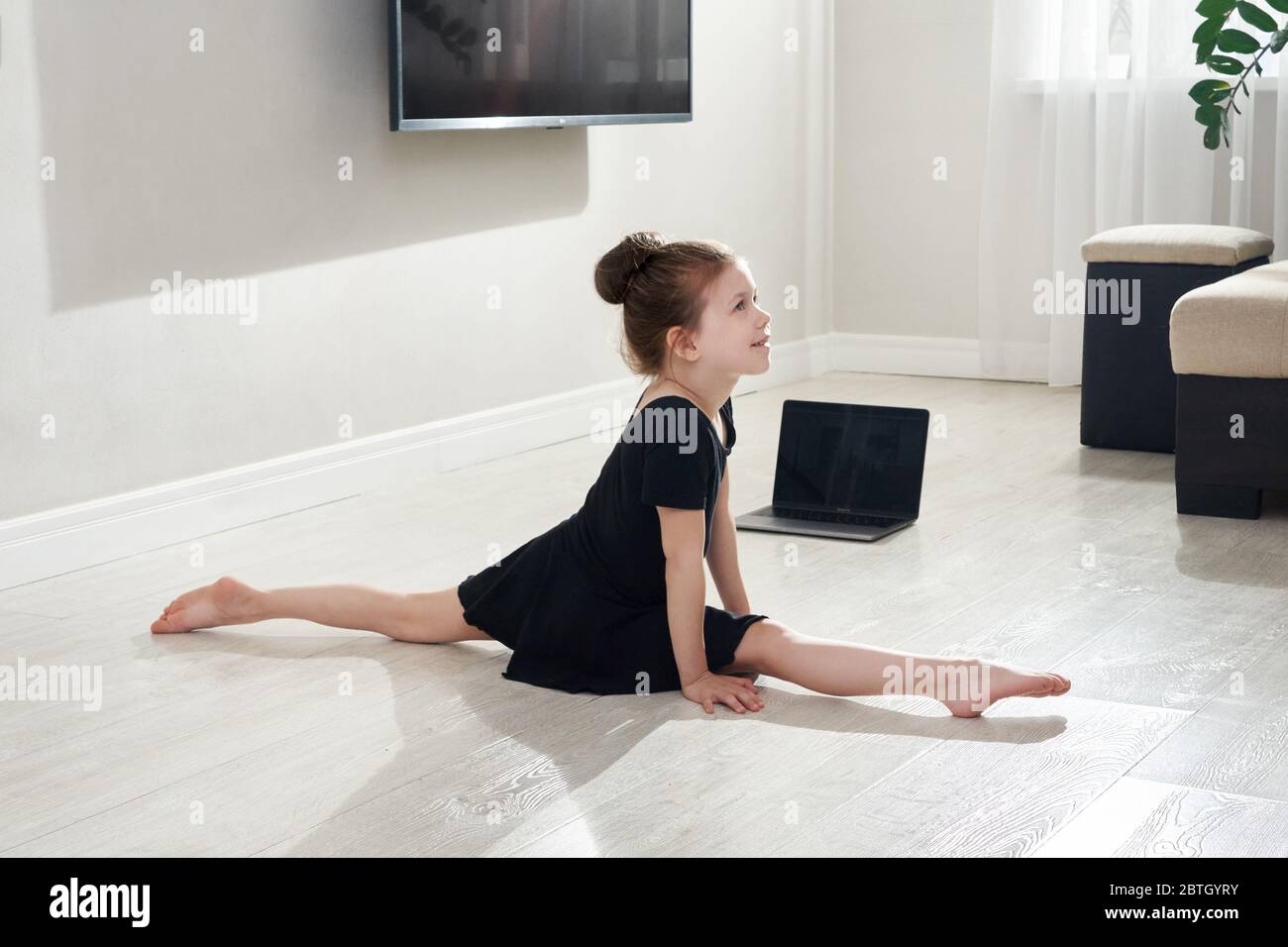 Little girl doing gymnastics exercises at home using online learning ...