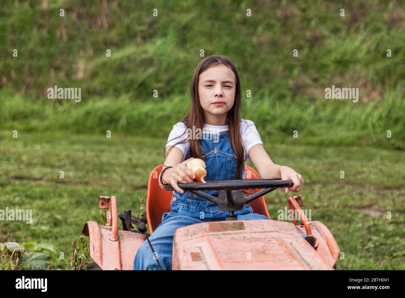 Young girl sitting on tractor in a green farm field Stock Photo - Alamy