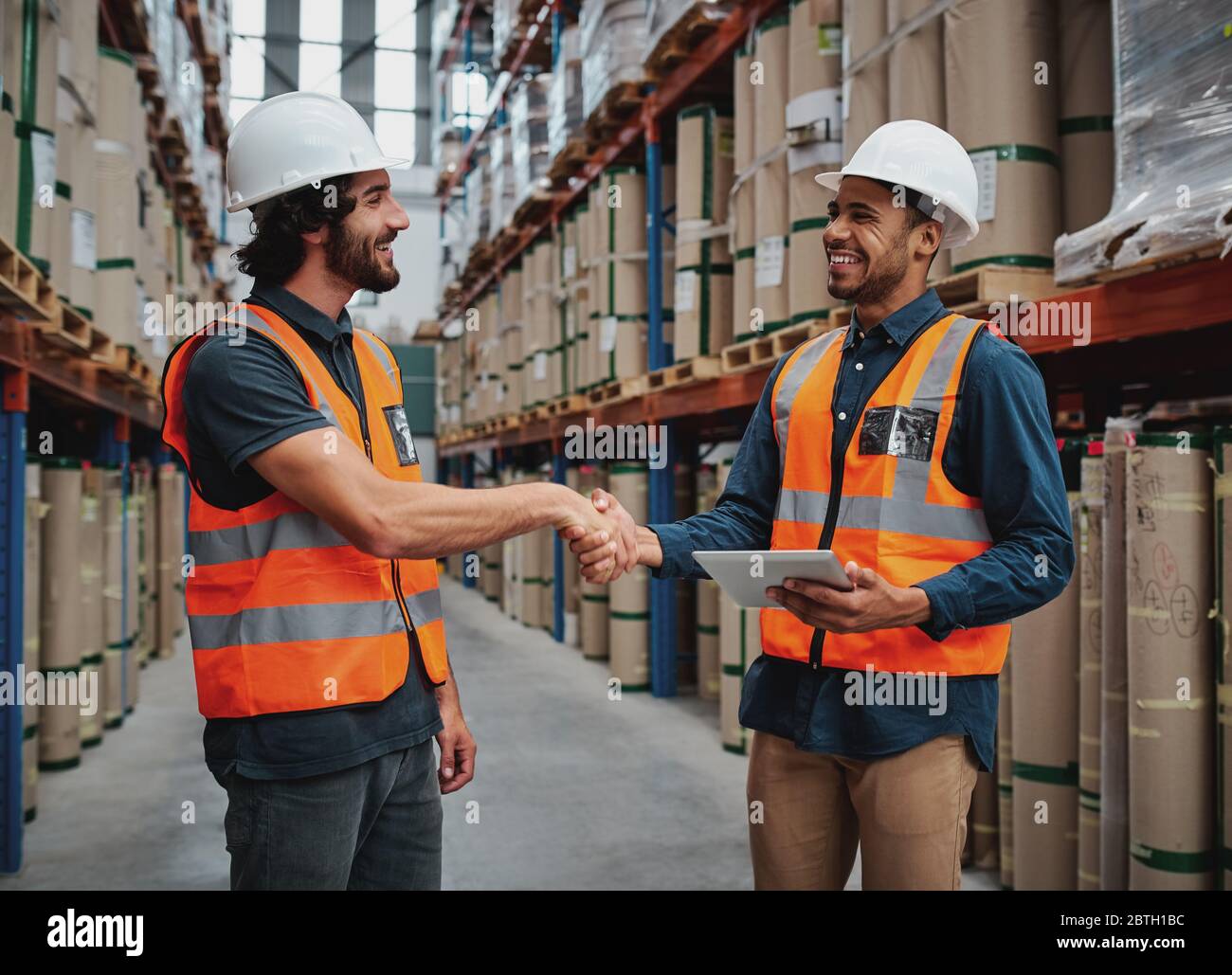 Two cheerful man making a firm handshake in logistics workhouse holding ...