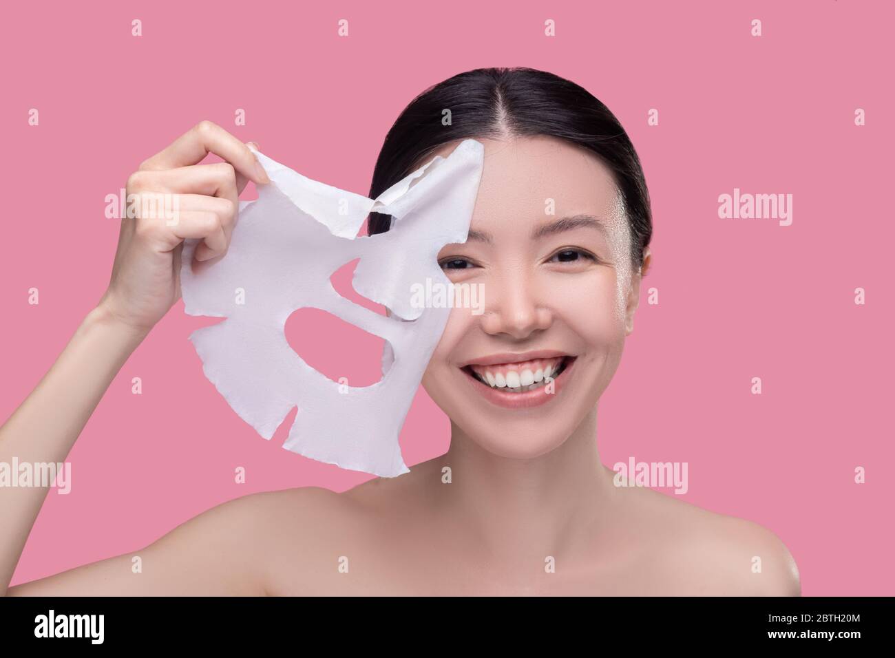 Smiling dark-haired asian girl taking off the facial mask Stock Photo ...