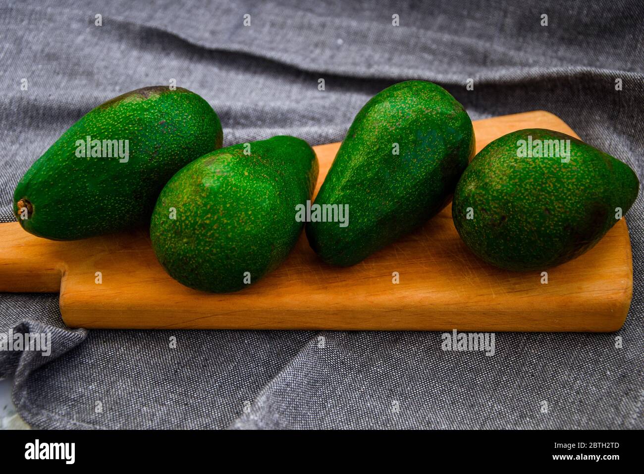 whole green avocado on the wooden tray and grey kitchen towel Stock ...