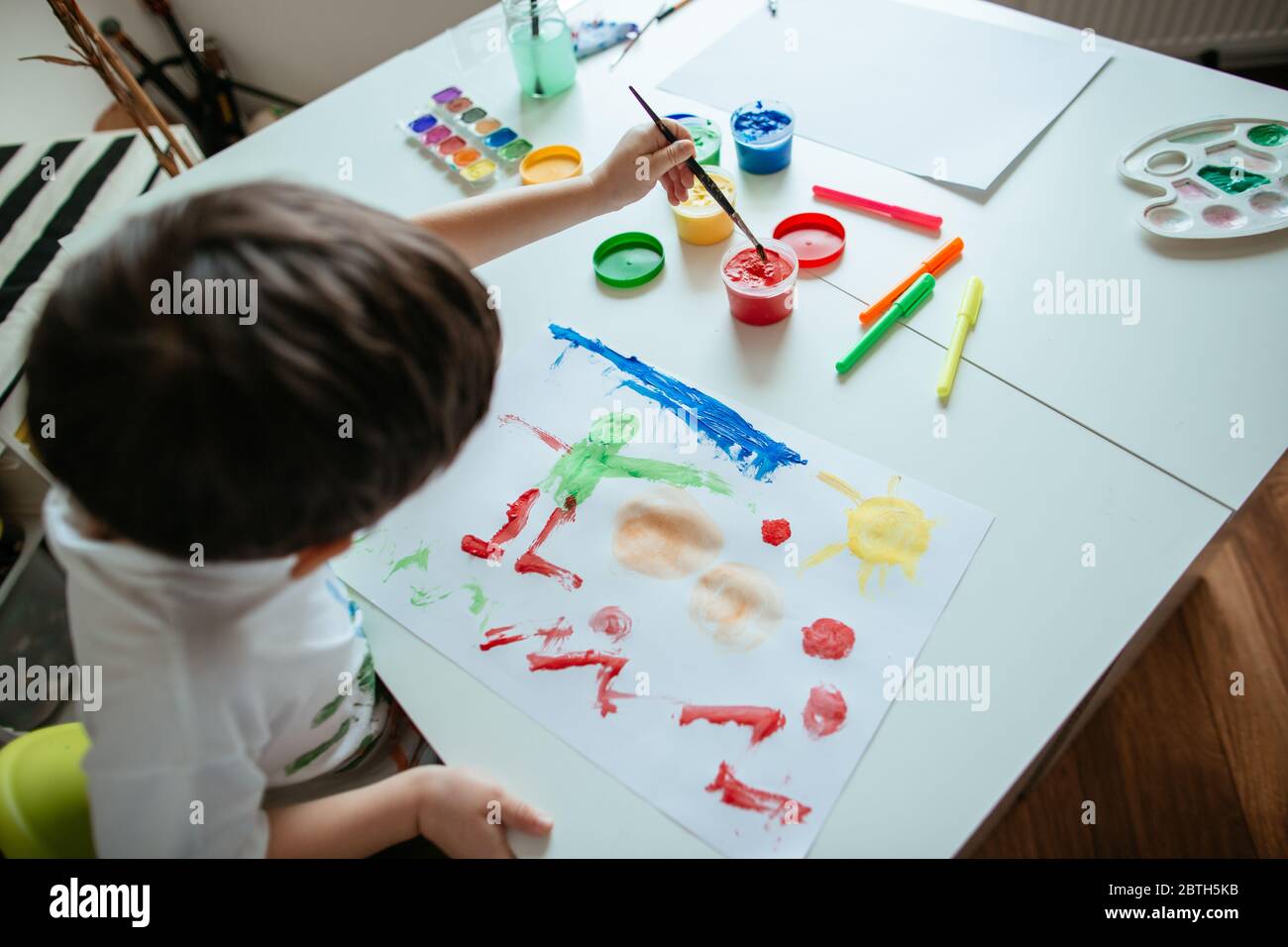 Left handed 5 year old boy reaching for red paint with paintbrush. Top ...