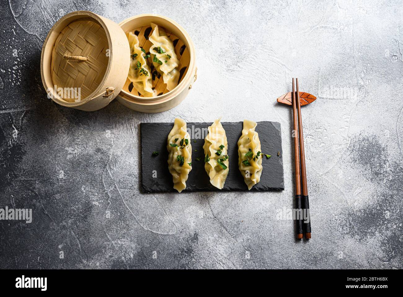 Boiled and hot chinese dumplings in wooden steamer and on black stone ...
