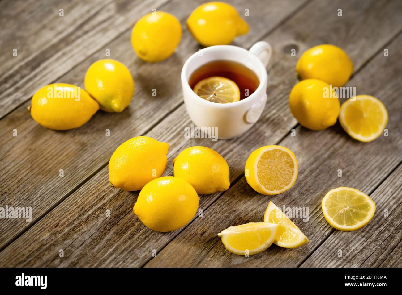 Cup of black tea with lemon slice and plenty of lemons around on grey ...