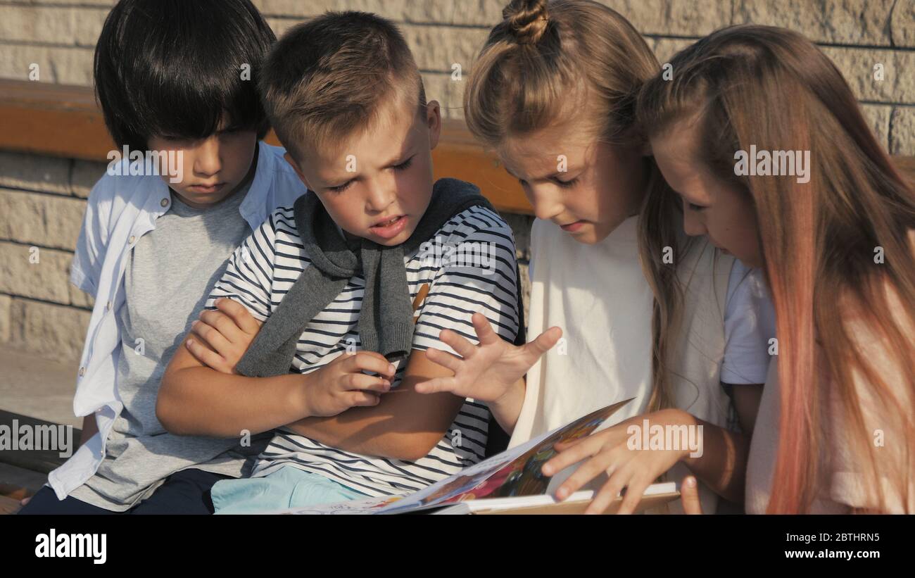 Kids looking at pictures in the book outdoors Stock Photo - Alamy