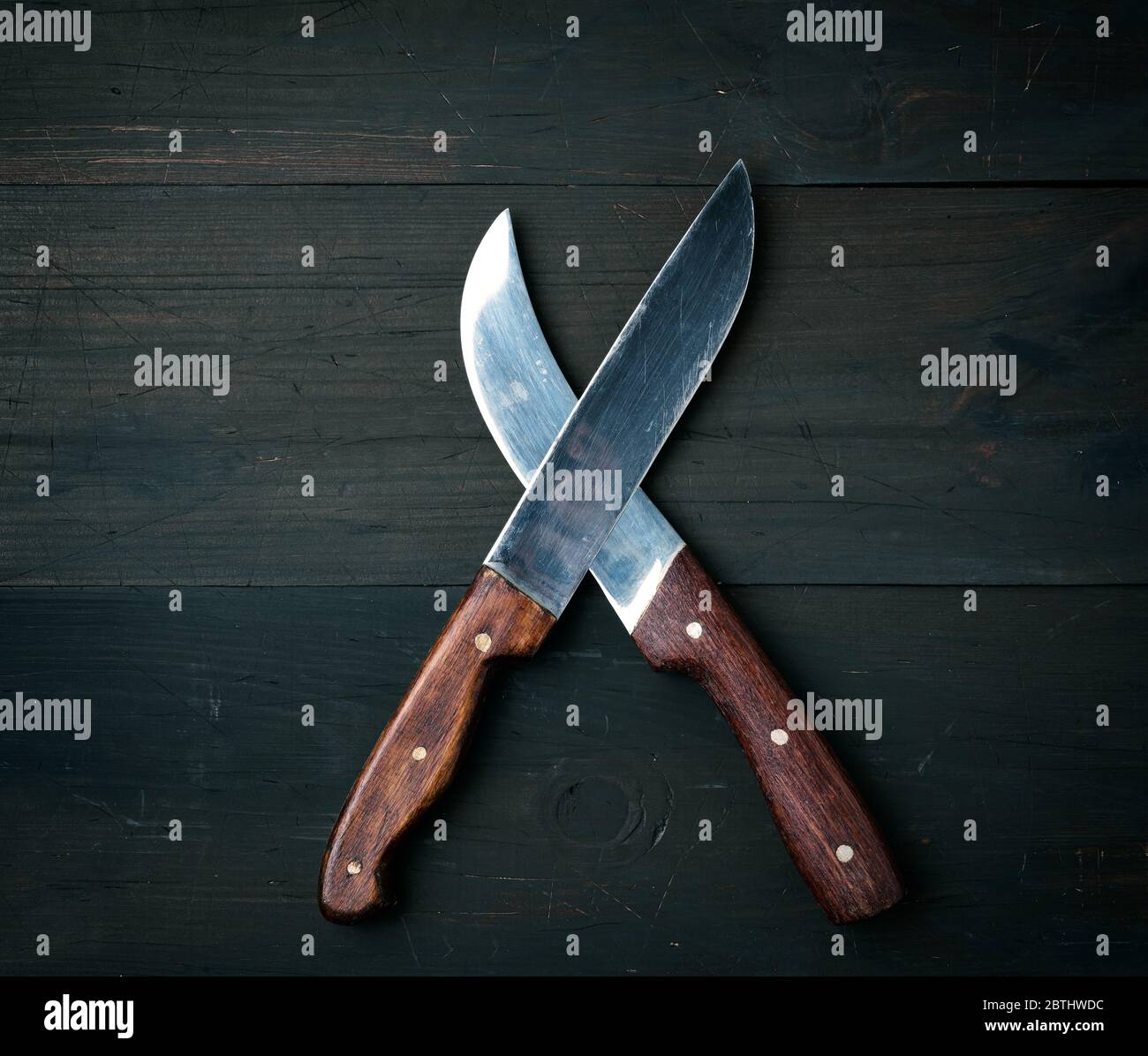 two sharp knives lie on a brown wooden surface, kitchen items are ...
