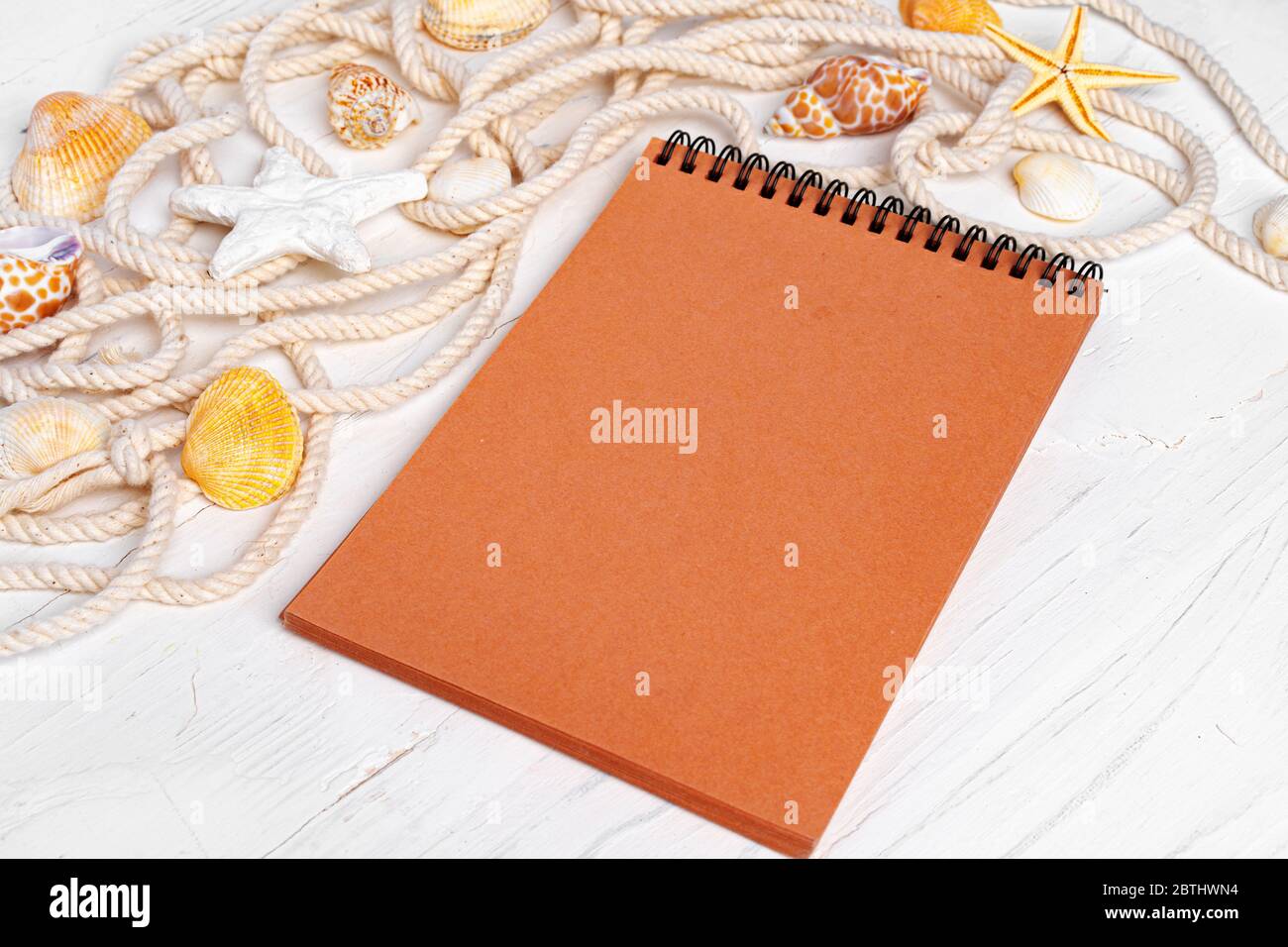 Close up photo of brown notepad with sea shells on wooden planks ...