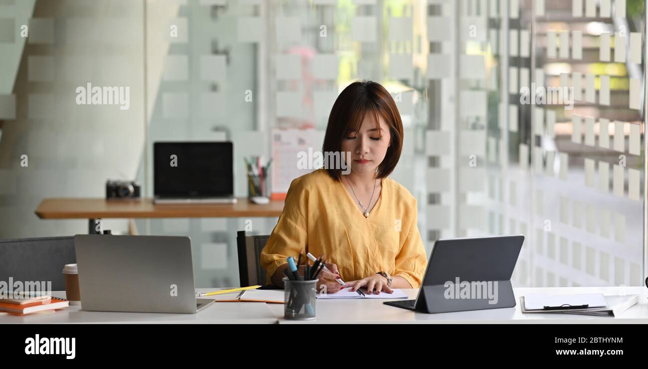 Photo of beautiful woman writing on paperwork while sitting in front ...