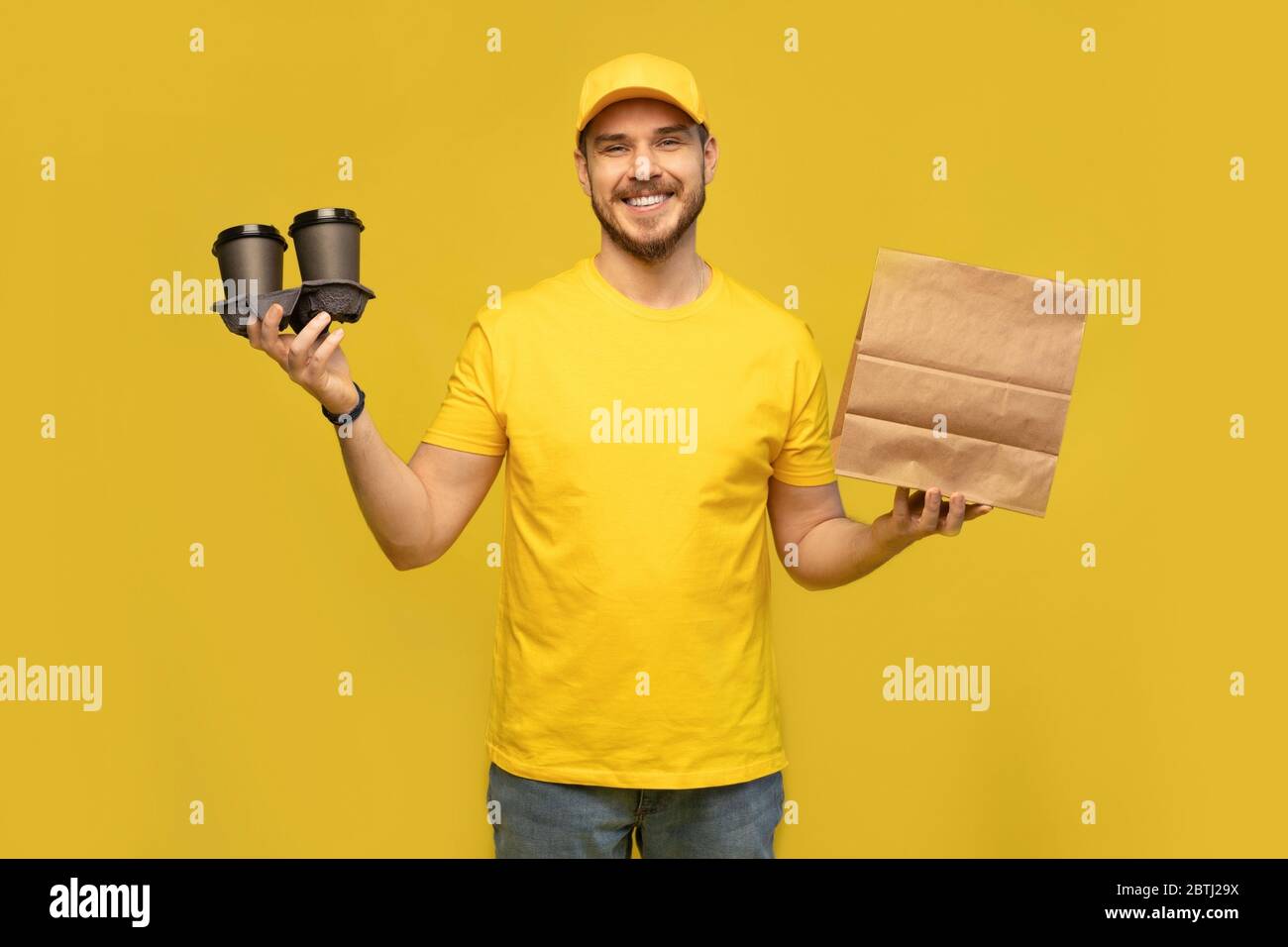 Portrait of young delivery man in yellow uniform with paper packet and ...