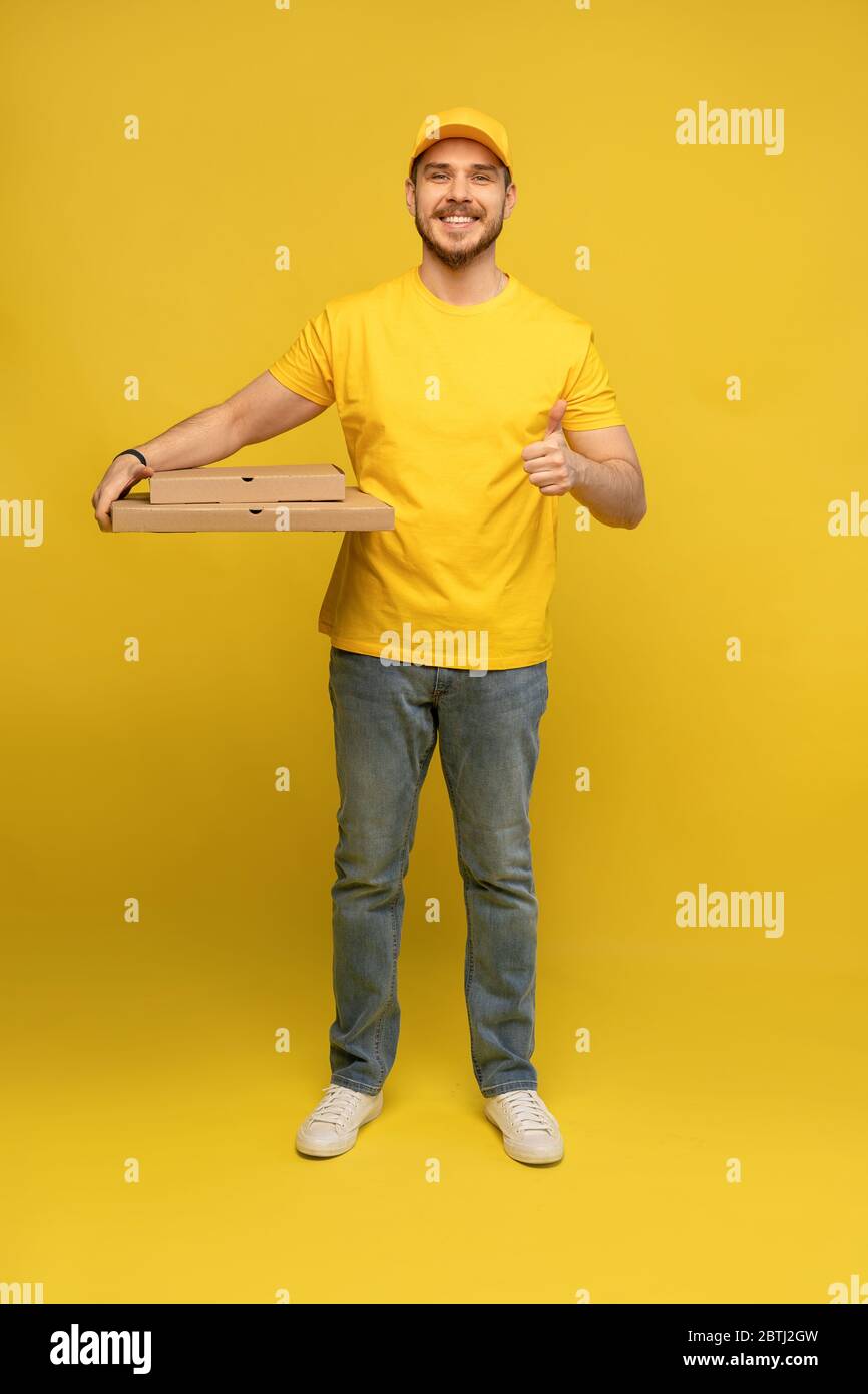 Portrait of young delivery man in yellow uniform with pizza boxes ...