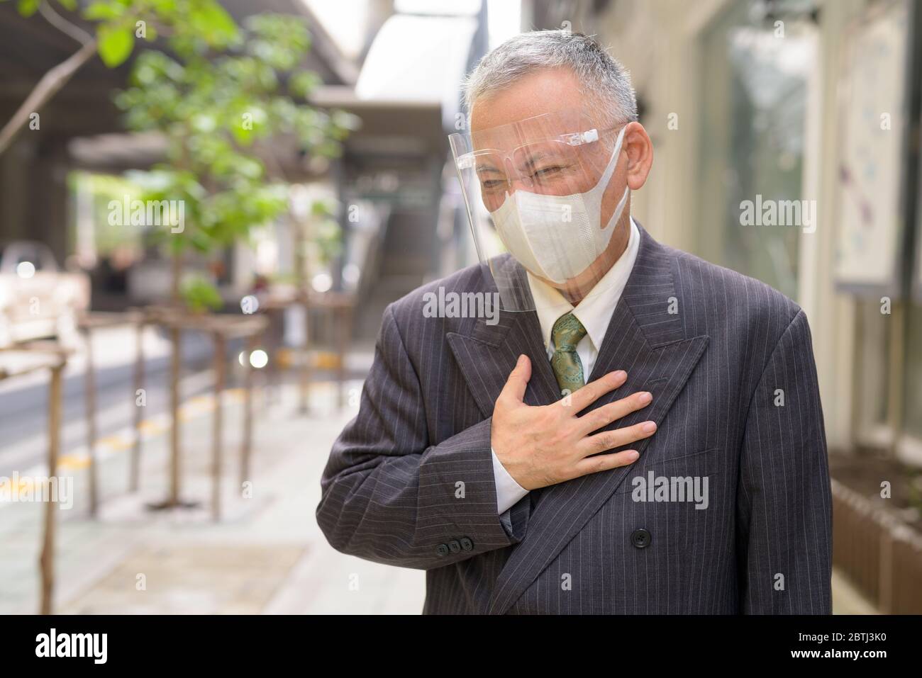 Stressed mature Japanese businessman with mask and face shield getting ...
