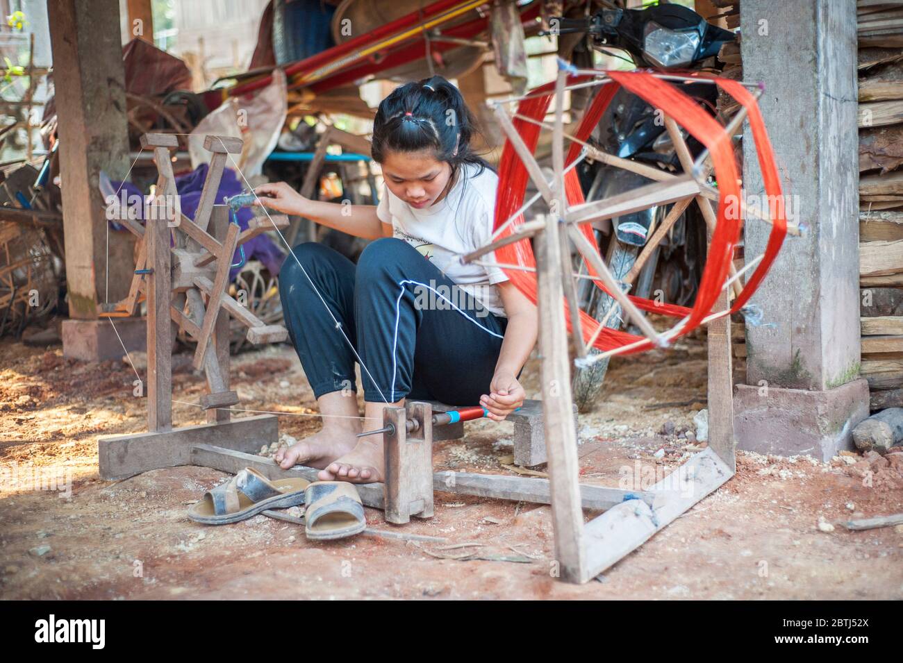 A Laotian woman spins thread on a simple wooden spinning wheel ...