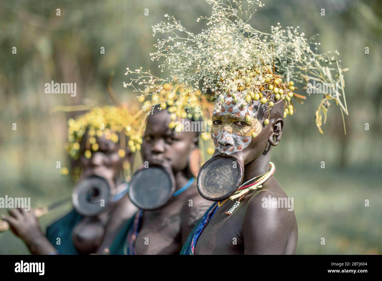 Three tribes people in line wearing clay plates in their mouths ...