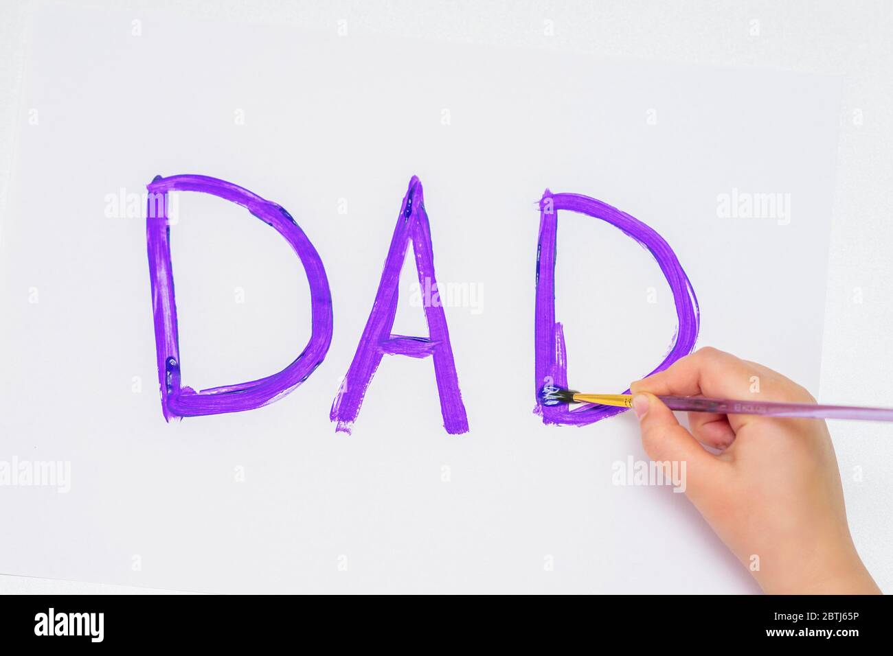 Top view of hand of child drawing purple word Dad on white paper. Happy ...
