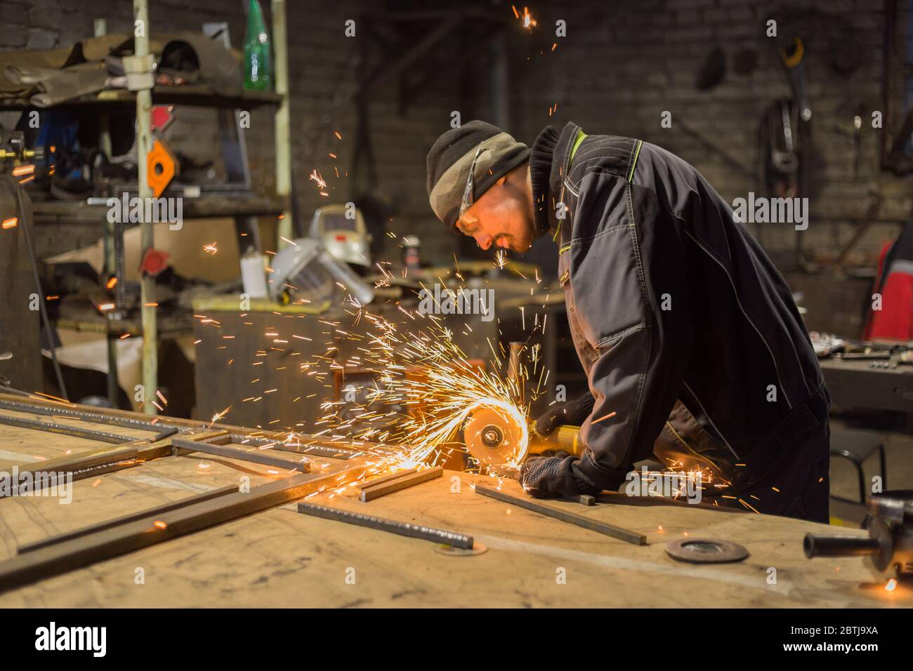 Professional blacksmith sawing metal with hand circular saw at forge ...