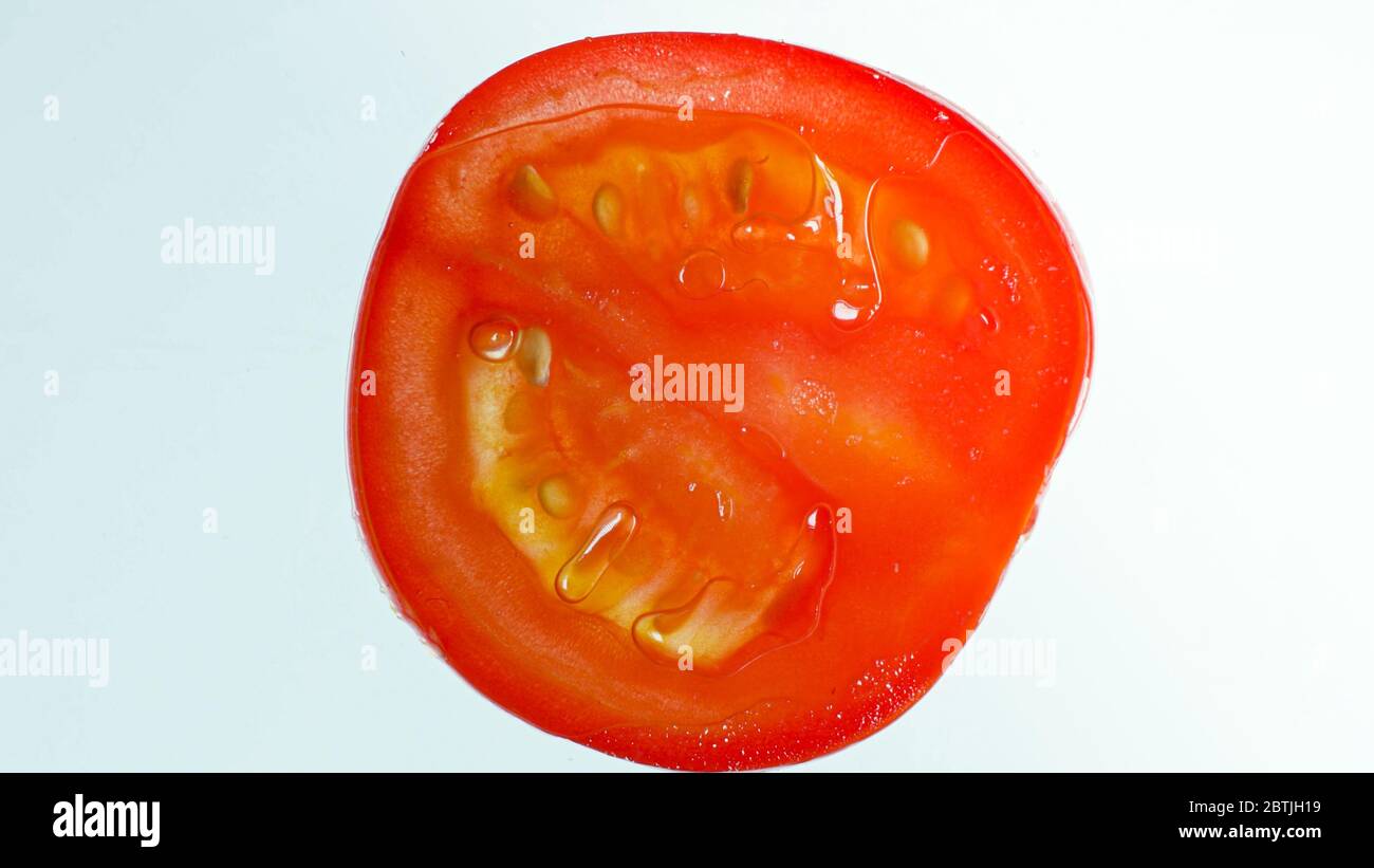 Closeup image of red tomato slice in water over white background ...