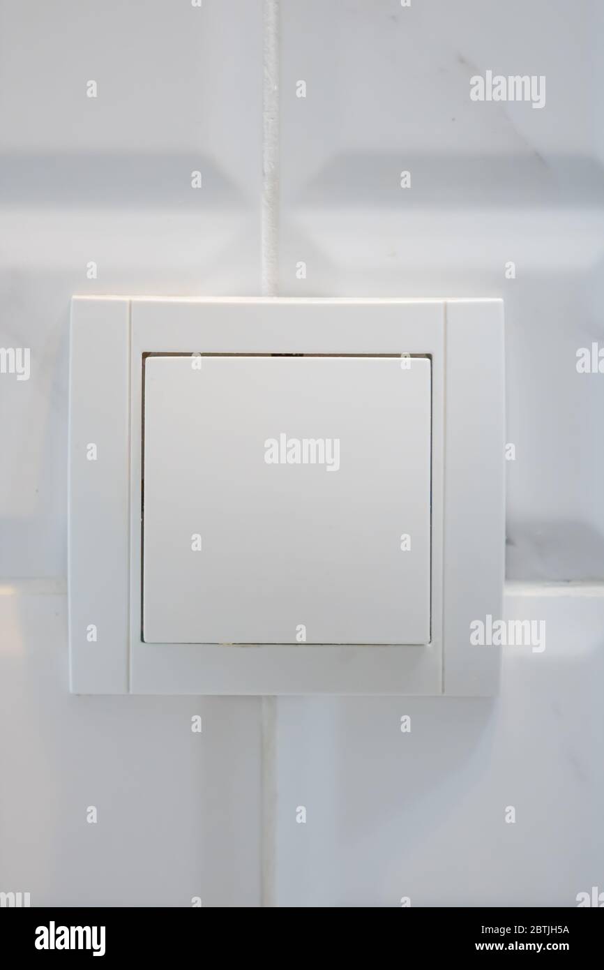 Close up view of white electric light switch on white tile. Building ...