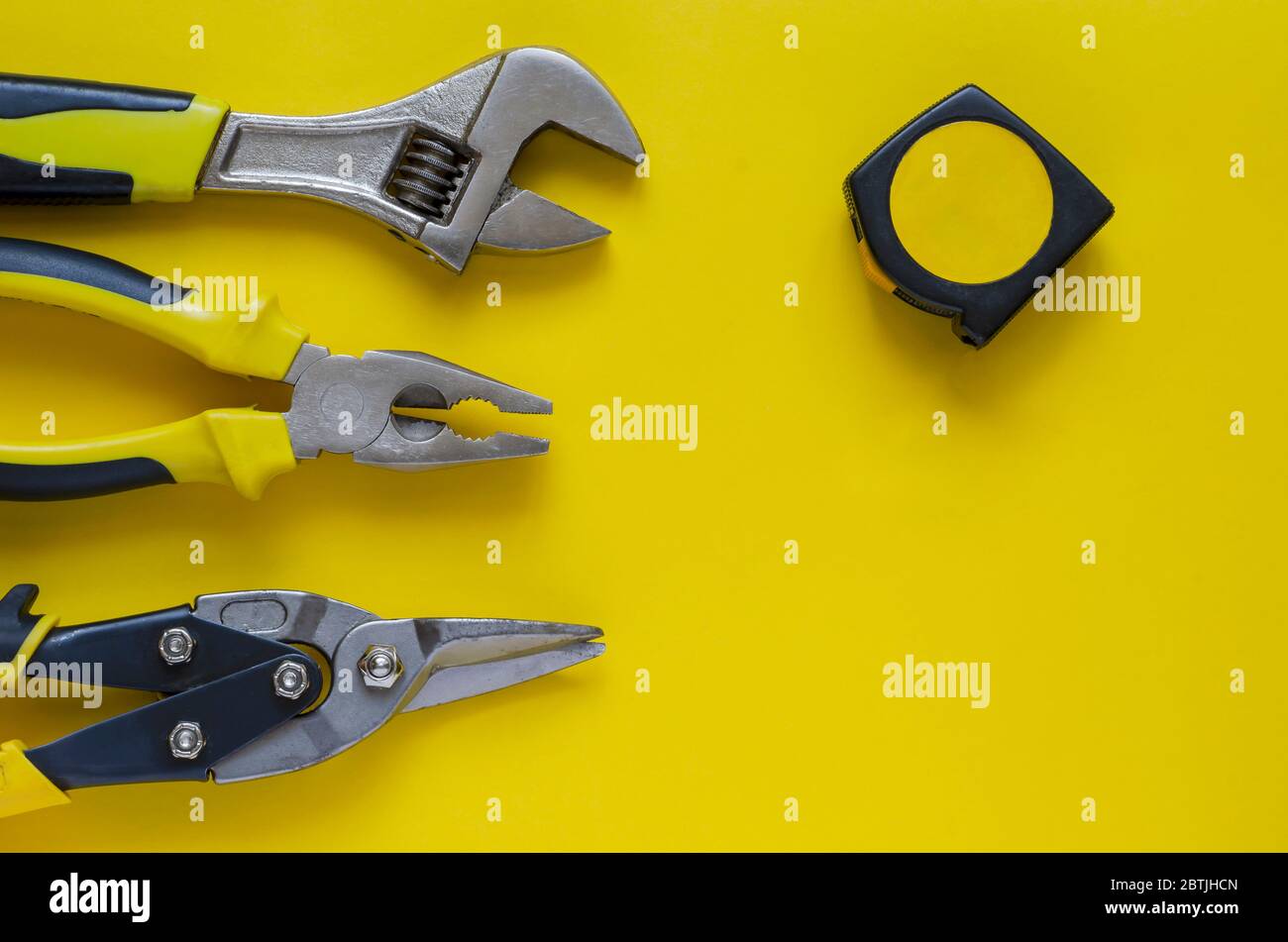Line of hand tools with black and yellow handles on a yellow background ...