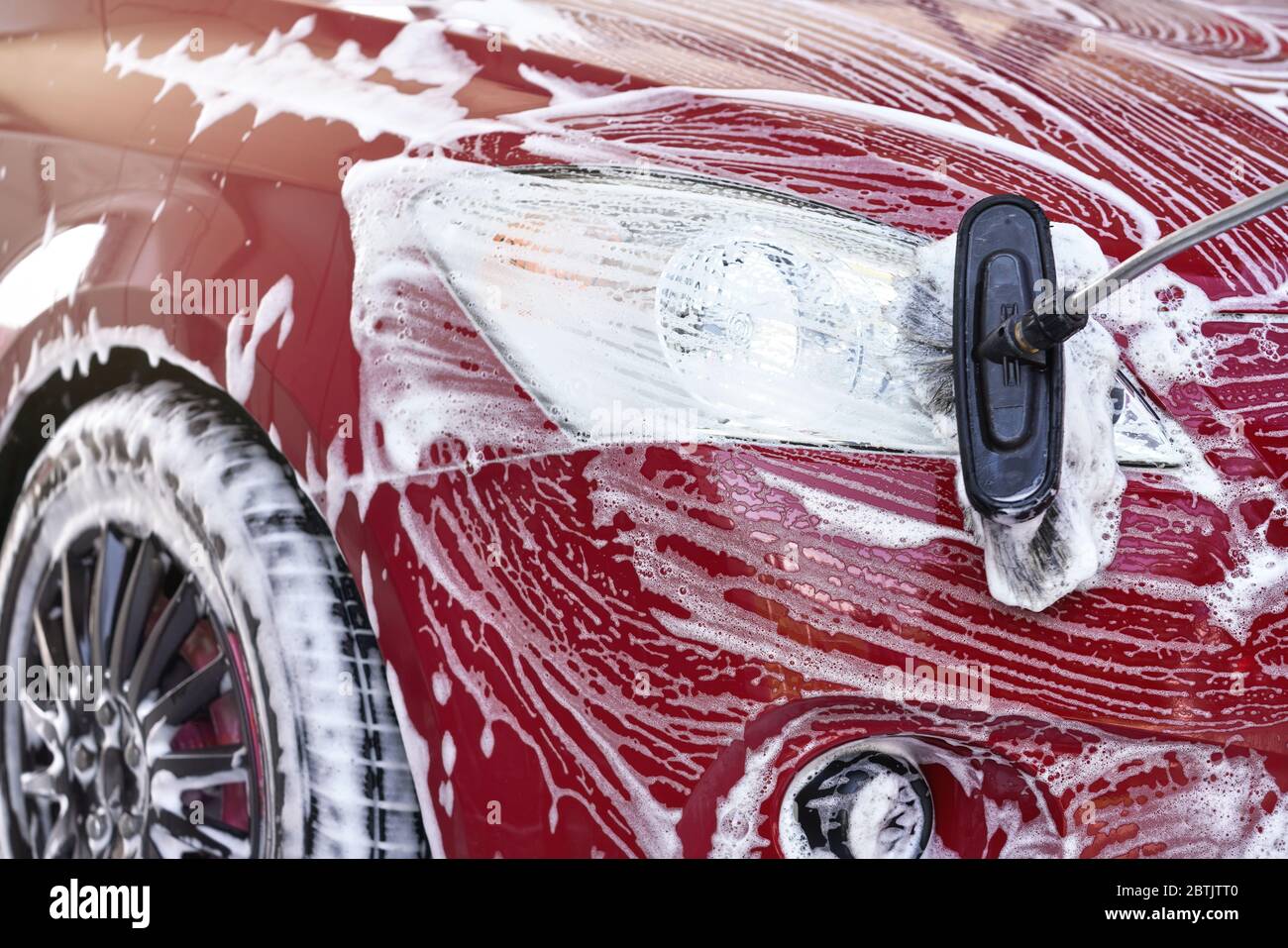 Detail on red car front light washed in self serve carwash, white soap ...